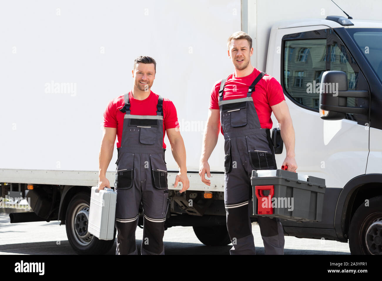 Portrait Of A Smiling Technicians Standing Against The Truck Holding ...