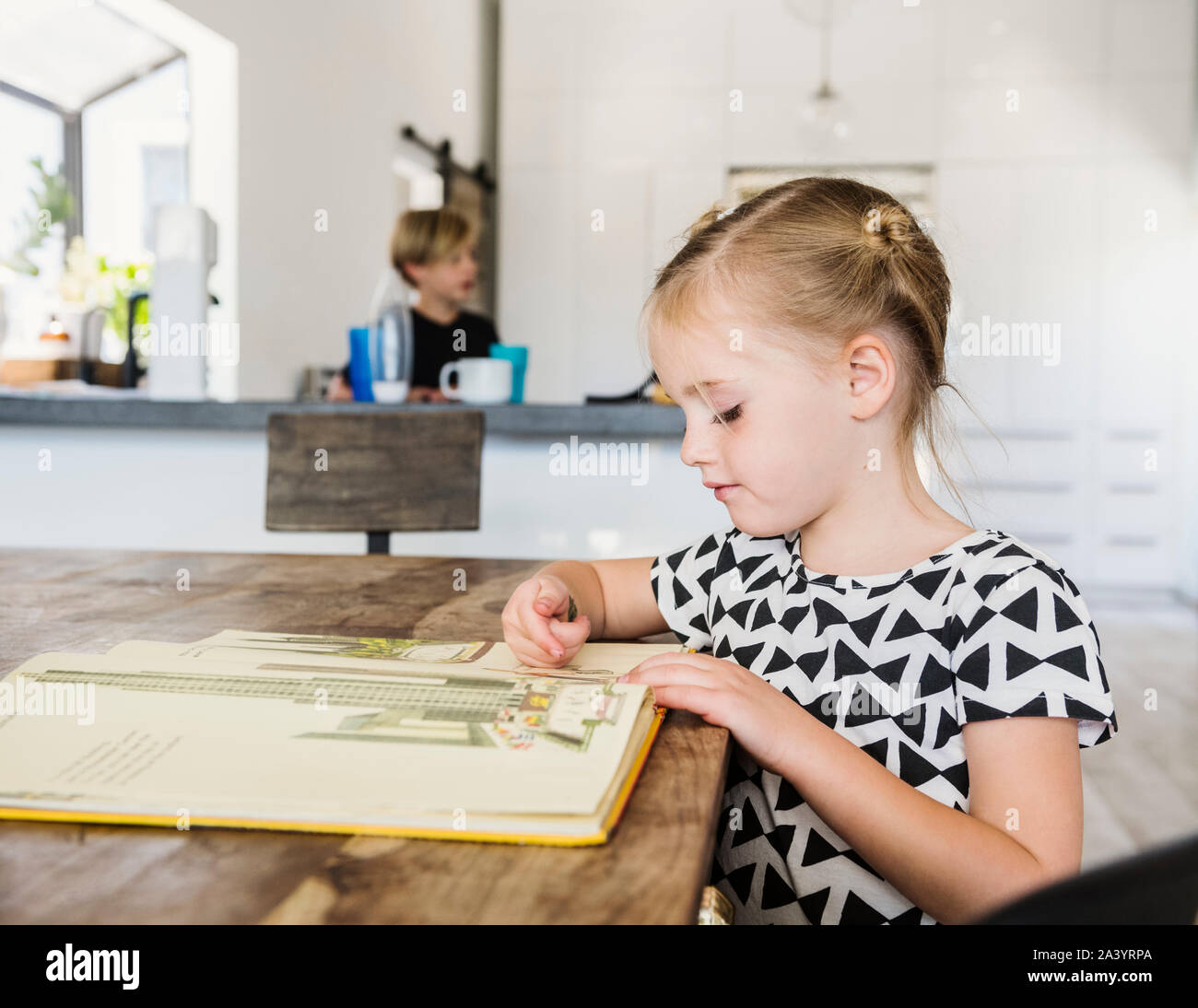 Girl reading picture book at dining table Stock Photo - Alamy