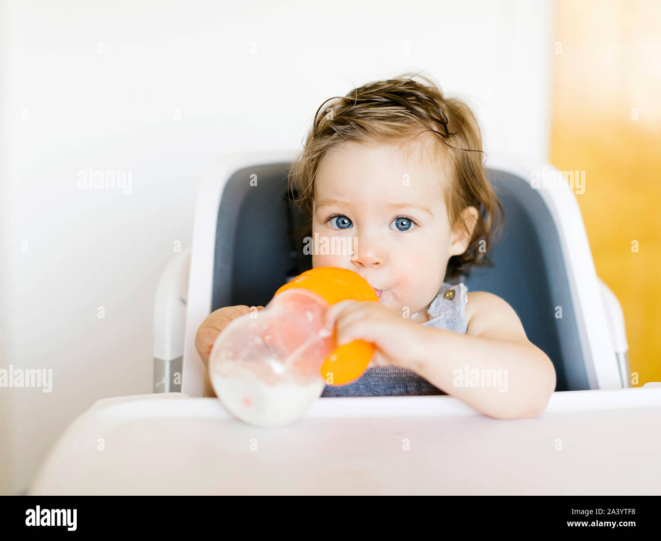 Baby girl drinking in high chair Stock Photo - Alamy