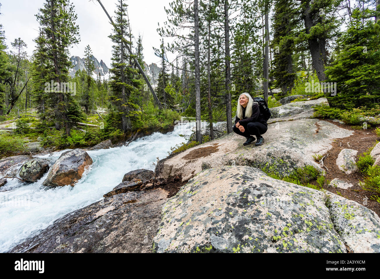 Mature woman crouching on rocks by river in Stanley, Idaho, USA Stock ...