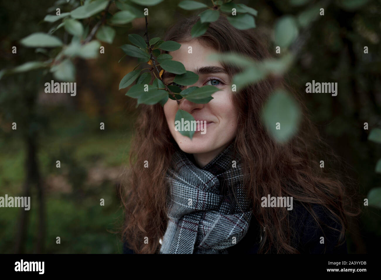 Young woman smiling behind tree branch Stock Photo - Alamy