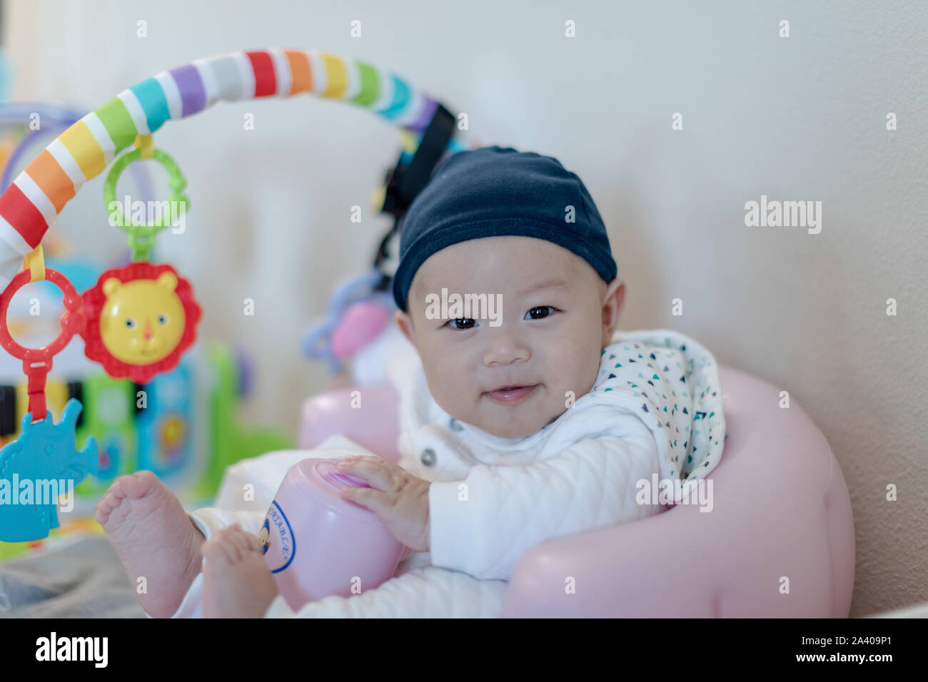Happy asian baby sitting pink chair behind toys at home. Looking at ...