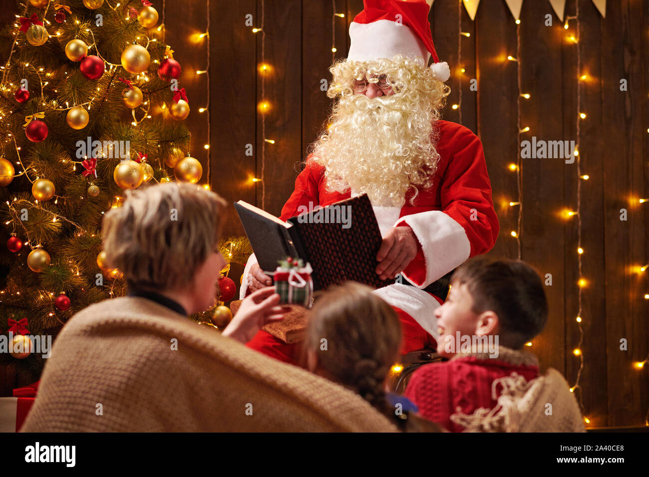 Santa Claus reading book for family. Mother and children sitting indoor ...