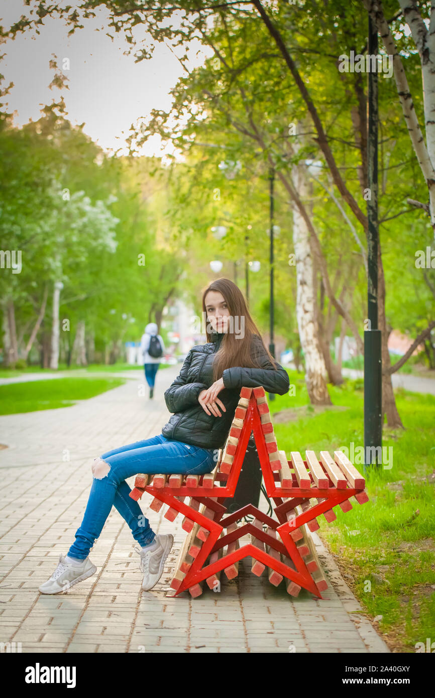 Young beautiful girl sits on a bench in the park. Lovely woman on the ...