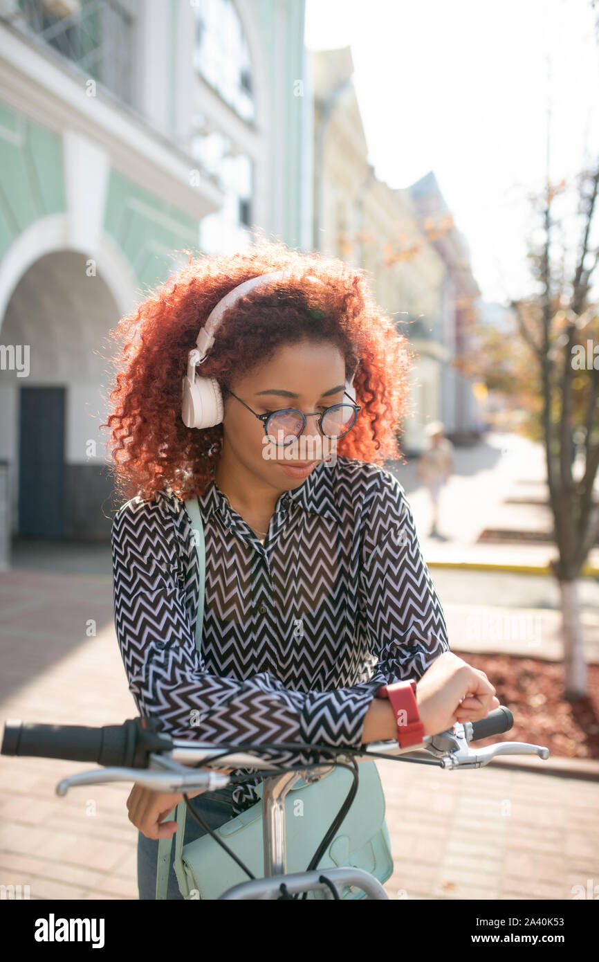 Curly red-haired student checking time while running late for classes ...