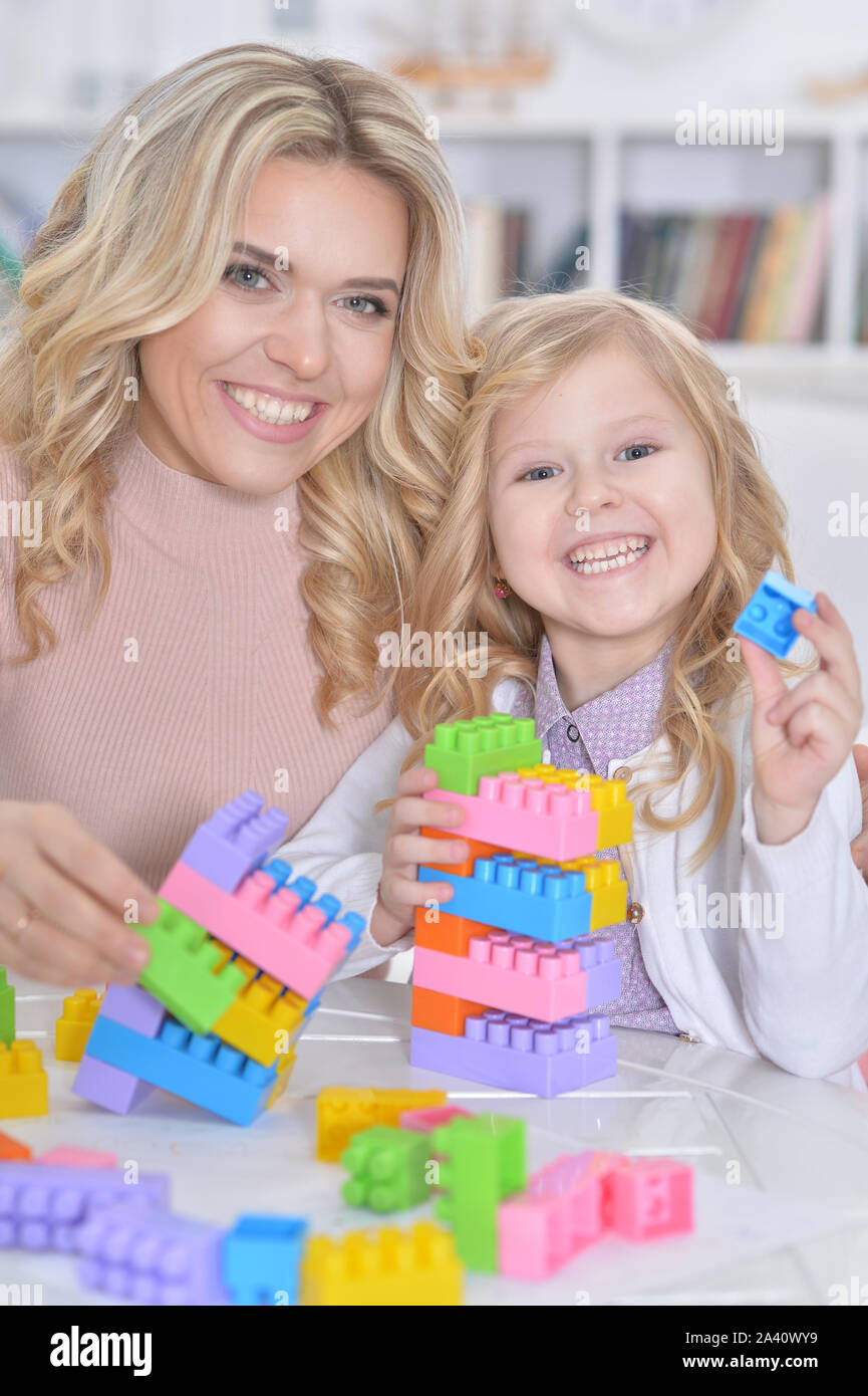 Little girl and her mother playing with colorful plastic blocks at home ...