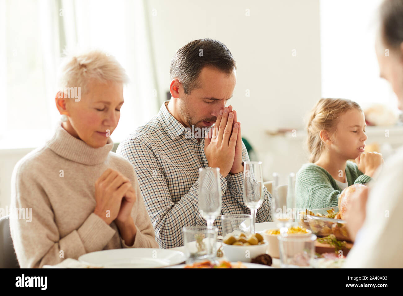 Family of three sitting at the table and praying together before the ...