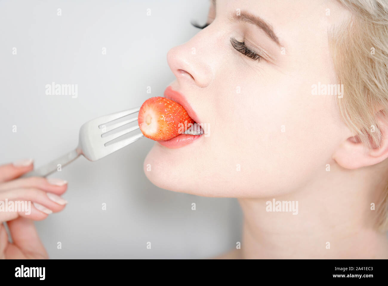 Beautiful young woman's face eating a strawberry Stock Photo - Alamy