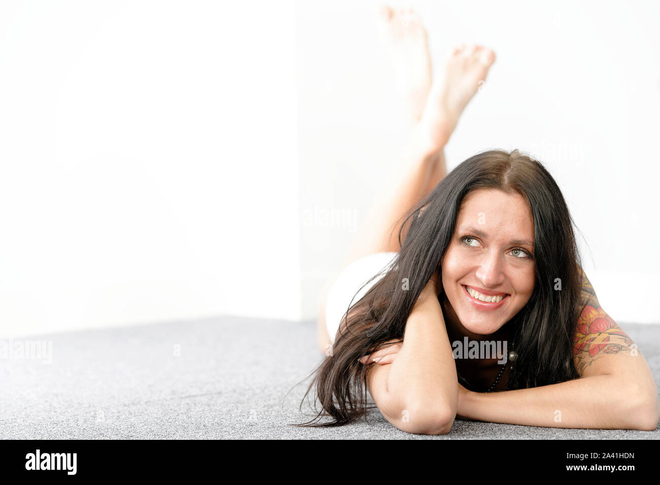 Beautiful young woman lying on her front on the floor smiling Stock ...