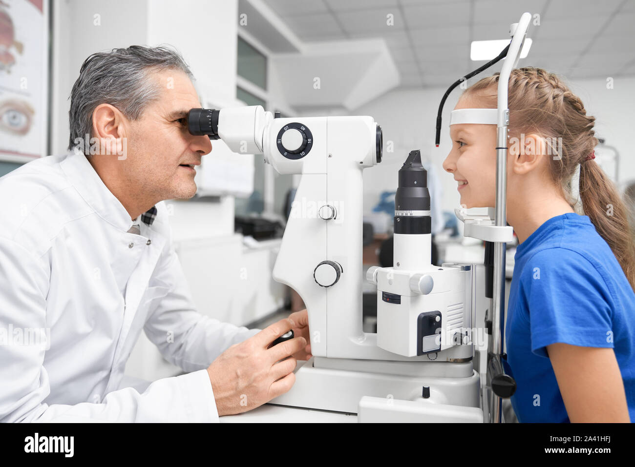 Side view of process of checking eyesight in clinic. Elder doctor ...