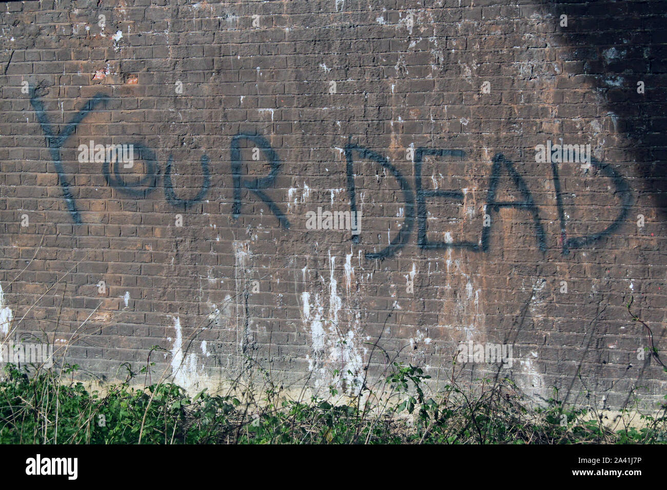 Badly spelt graffiti on a brick wall under bridge, You're Dead mispelt ...