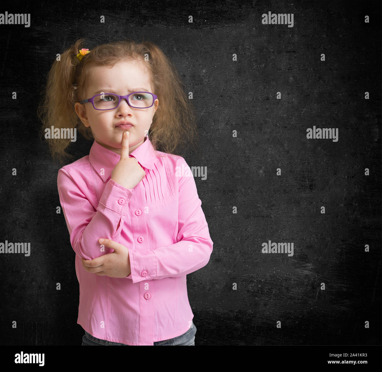 Serious kid standing and thinking near black chalkboard Stock Photo - Alamy