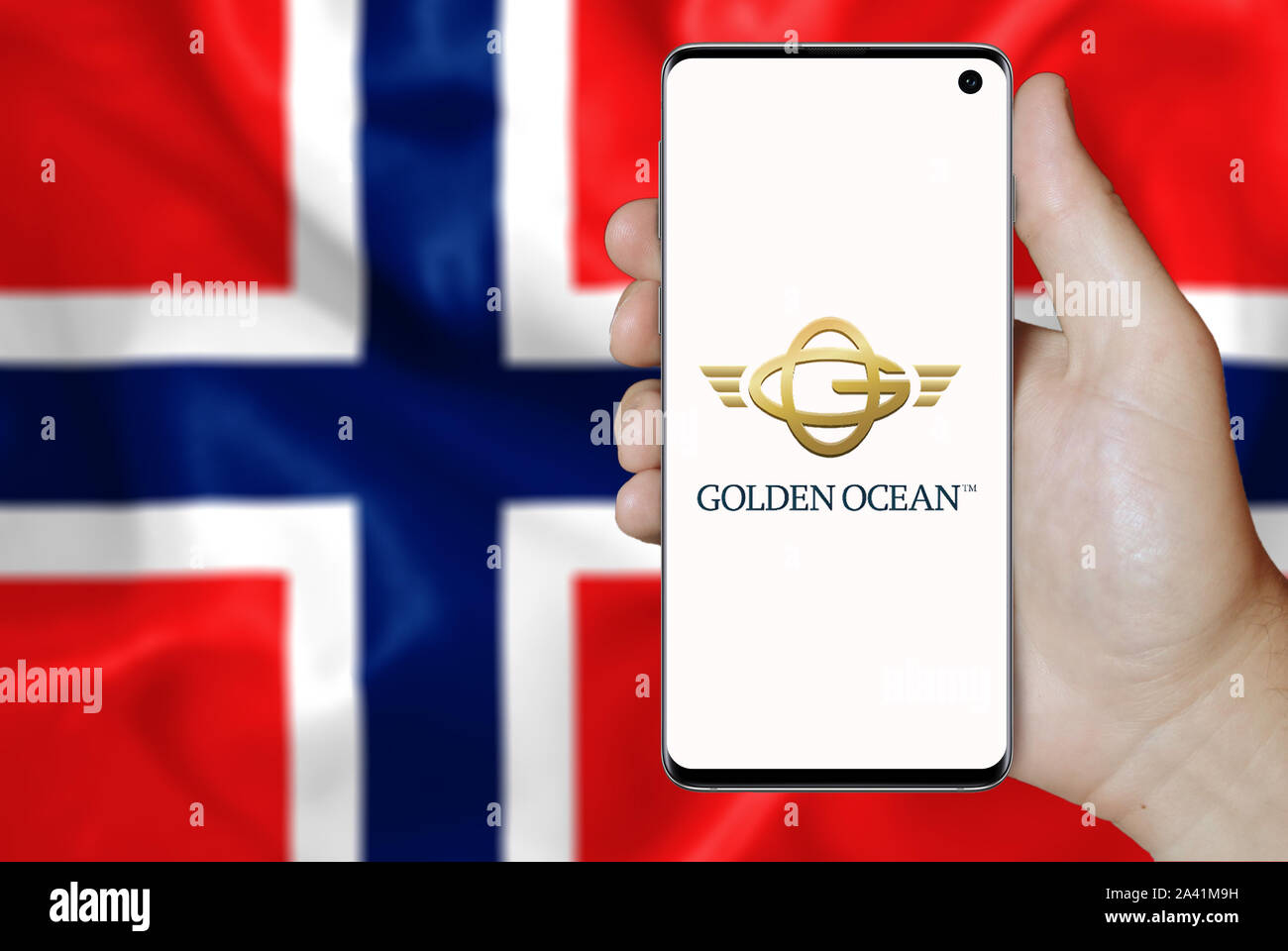 A man holds a phone displaying the logo of company Golden Ocean Group ...