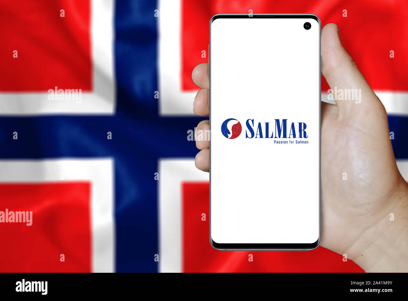 A man holds a phone displaying the logo of company SalMar listed on ...