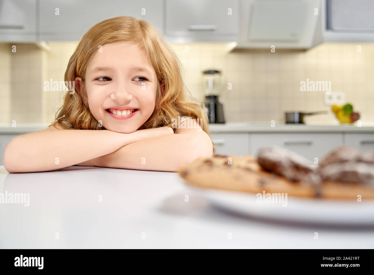 Selective focus of funny little girl sitting at kitchen, looking at ...