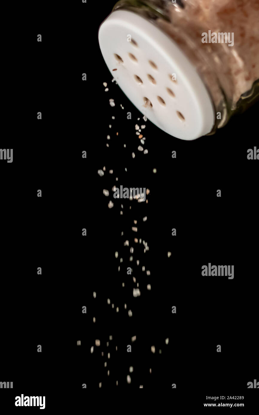 Pink himalayan salt falling out from a salt shaker on a black isolated ...