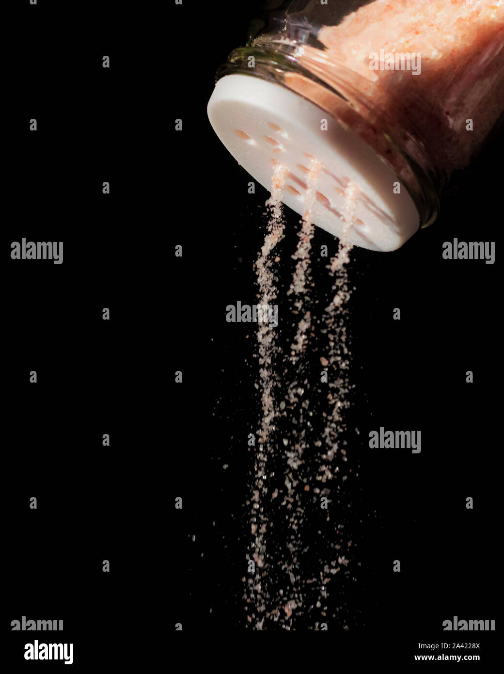 Pink himalayan salt falling out from a salt shaker on a black isolated ...