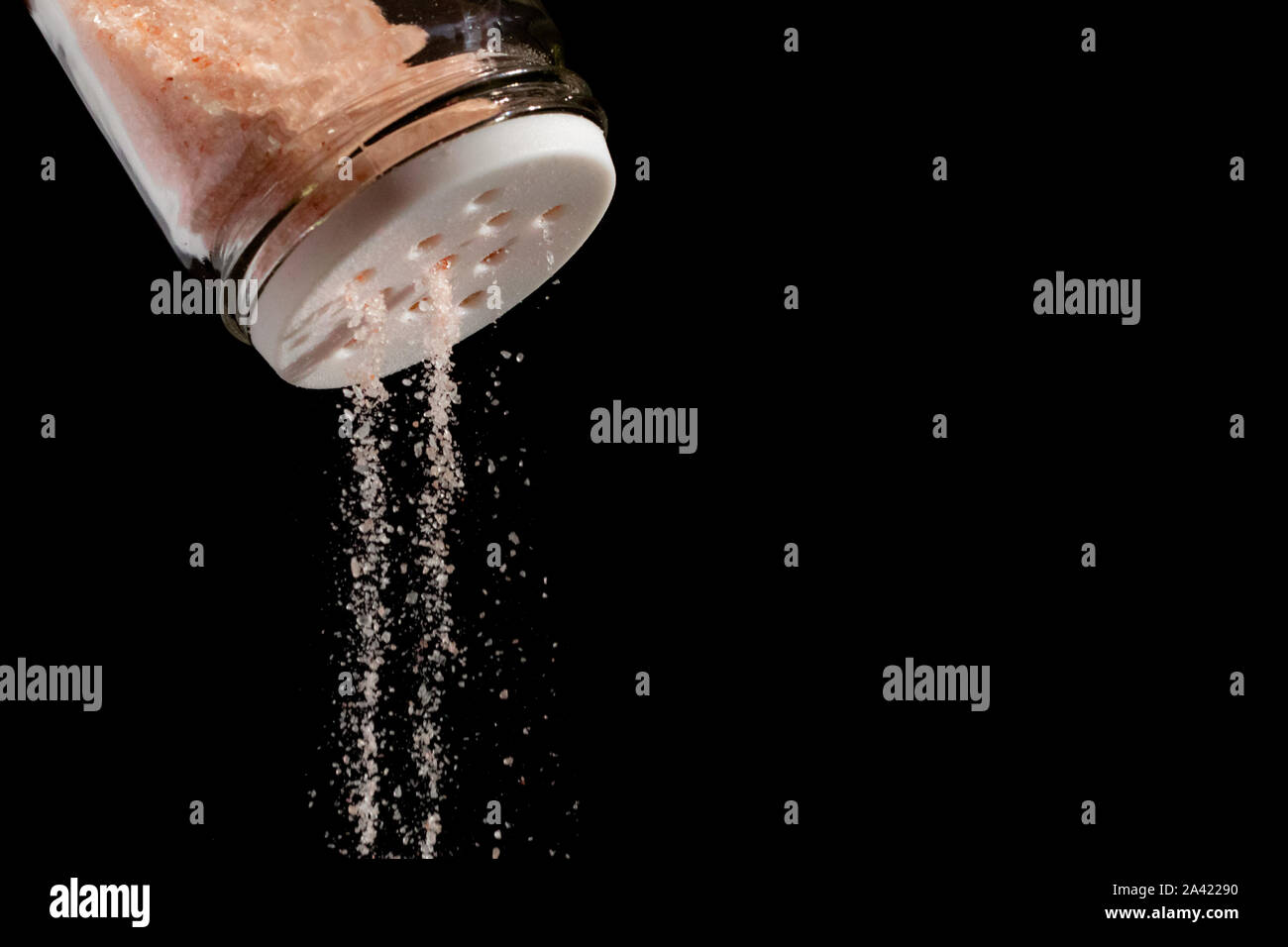 Pink himalayan salt falling out from a salt shaker on a black isolated ...