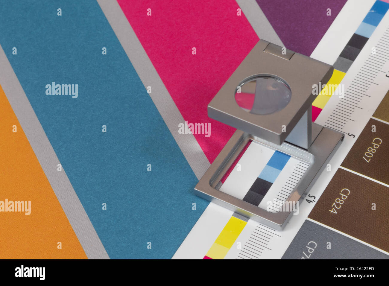 Silver magnifying glass standing on the test print, colored background ...