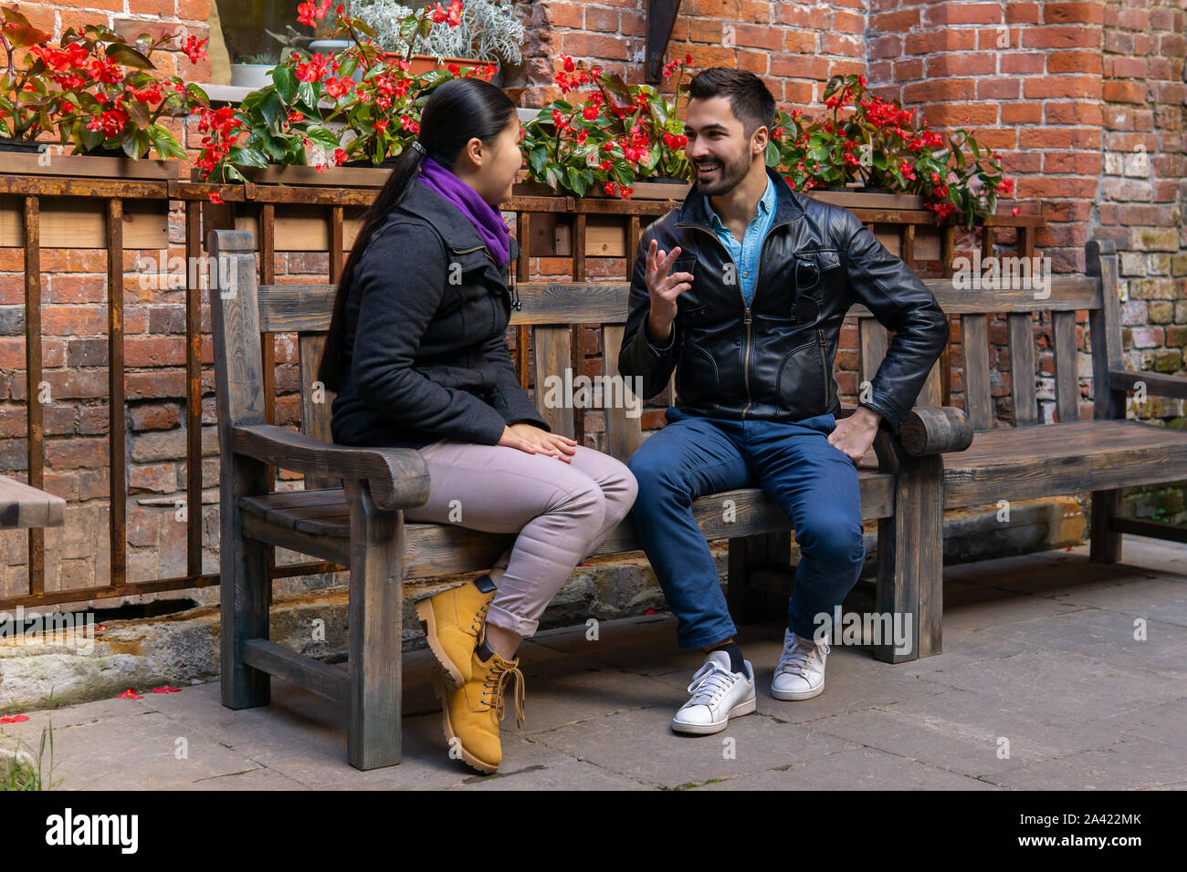 two young people a guy and a girl talking sitting on a bench outdoors ...