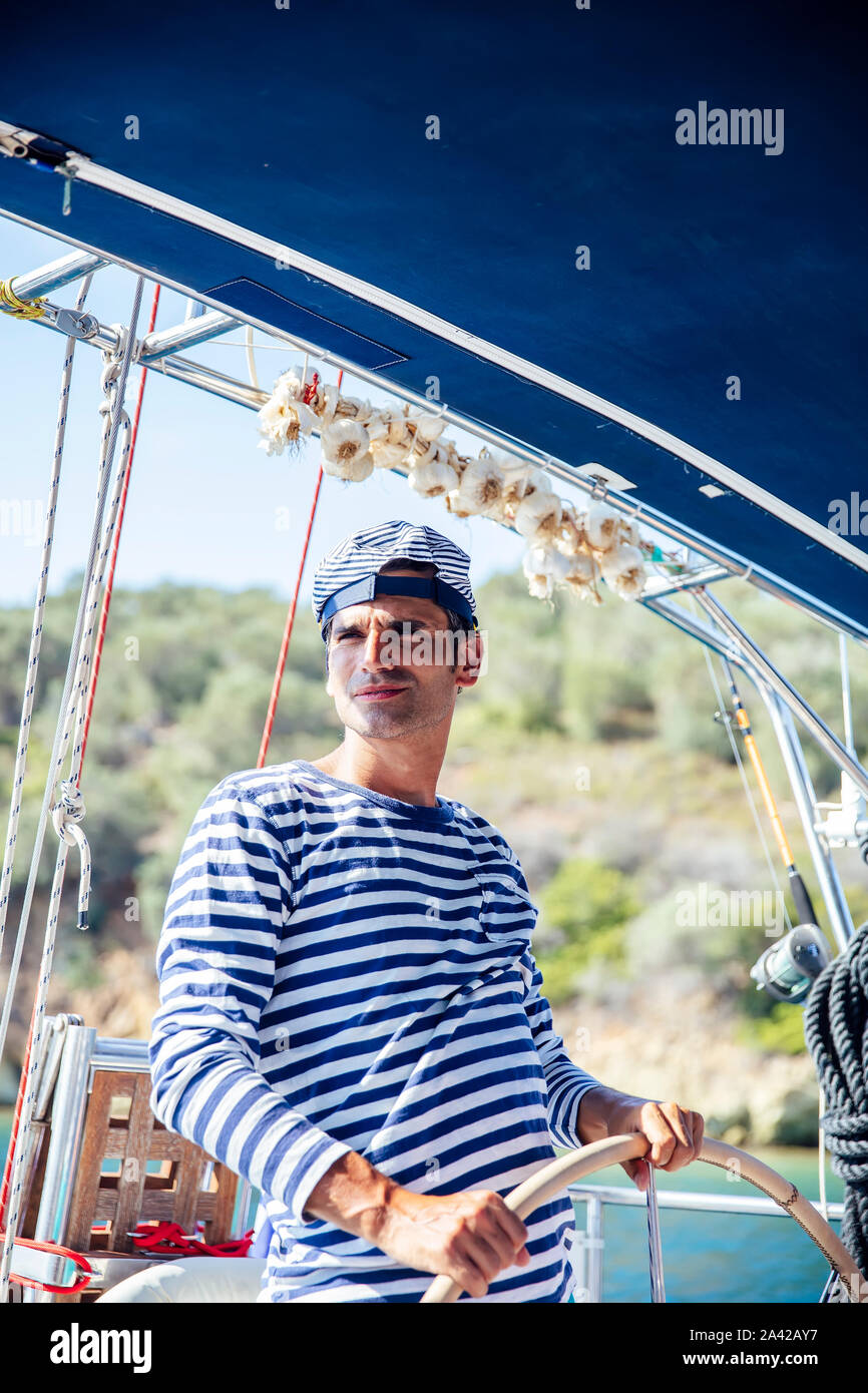 Handsome young man with captain cap on a sailboat at sea on a suuny day ...