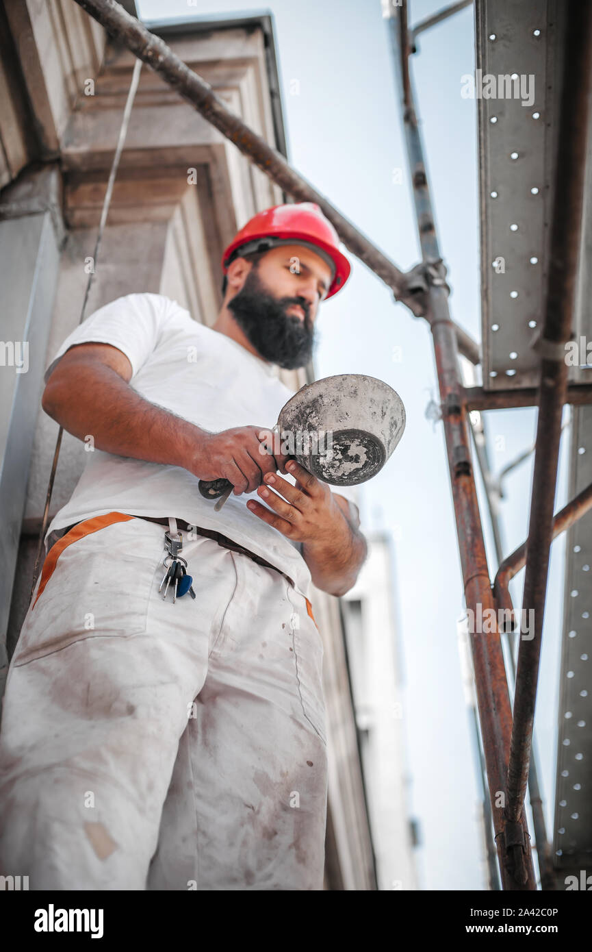 Construction mason worker on the scaffolding mixing cement and sand ...