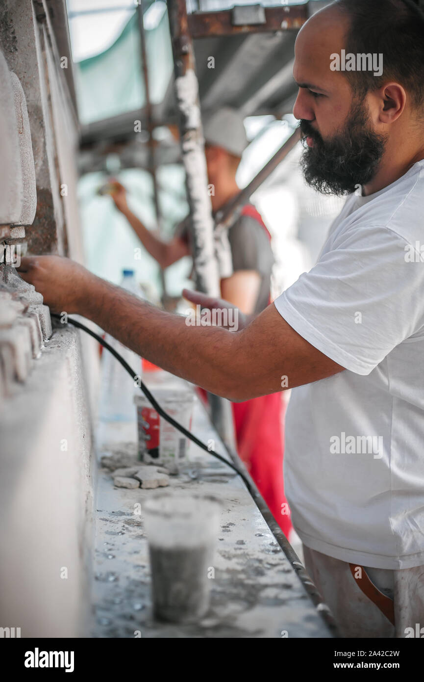 Construction mason worker on the scaffolding mixing cement and sand ...