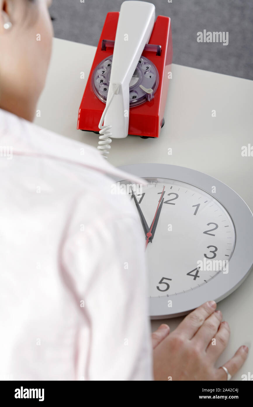 Woman watching the minutes pass on a clock at her desk waiting Stock ...