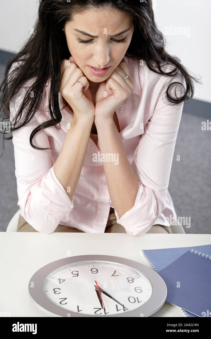 Woman watching the minutes pass on a clock at her desk waiting Stock ...