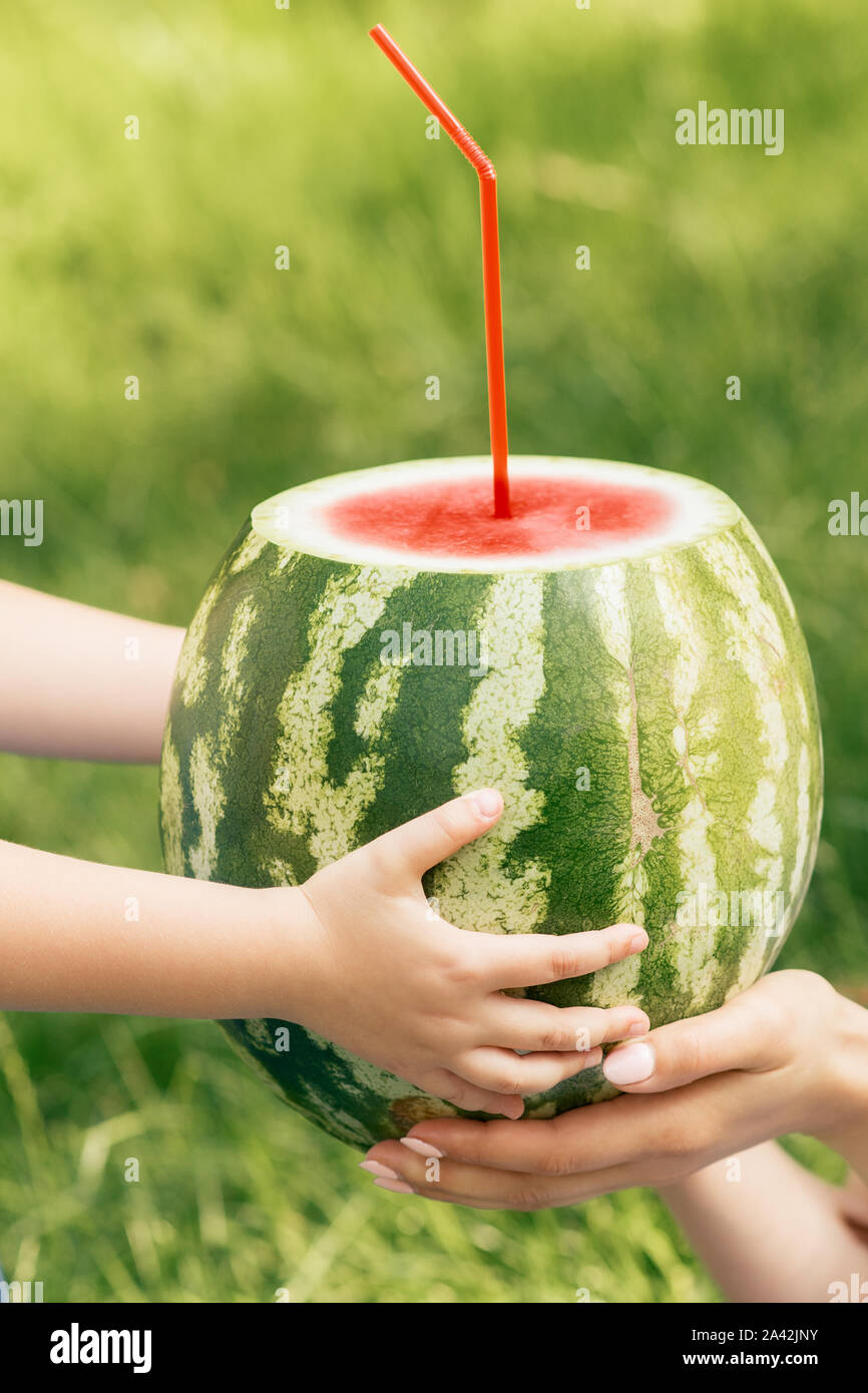Child's hands gives a juicy watermelon with a straw to female hands on ...