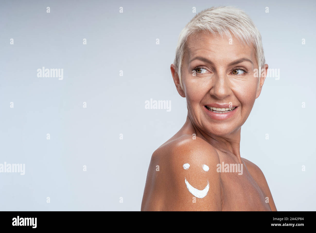 Have a look. Delighted female keeping smile on her face while standing ...