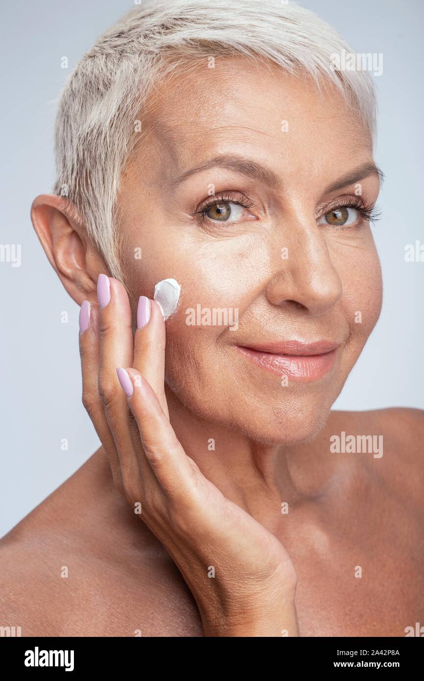 Natural beauty. Cute female expressing positivity while putting cream ...
