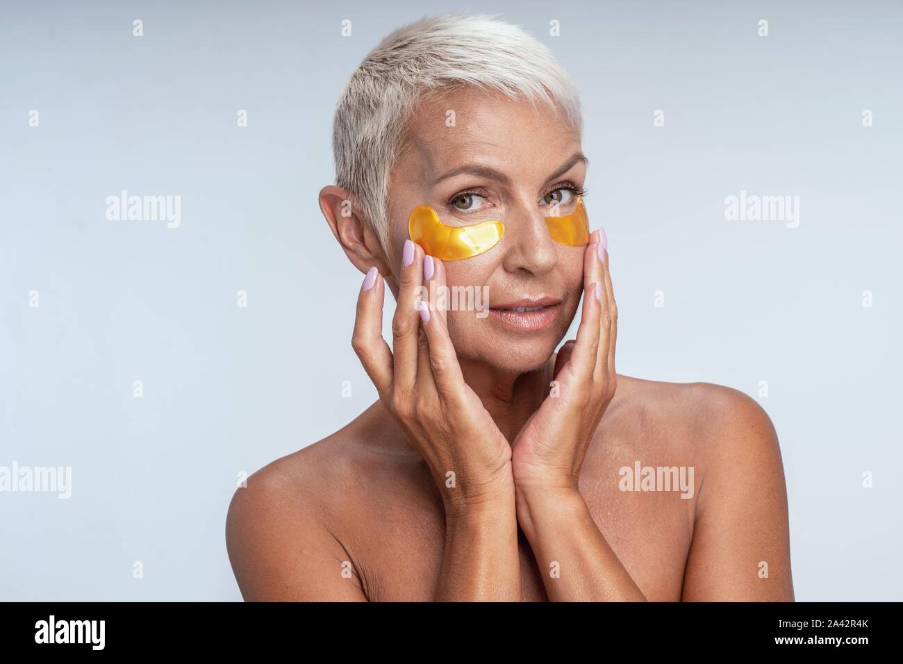 Delighted female touching her face while putting patches under eyes ...