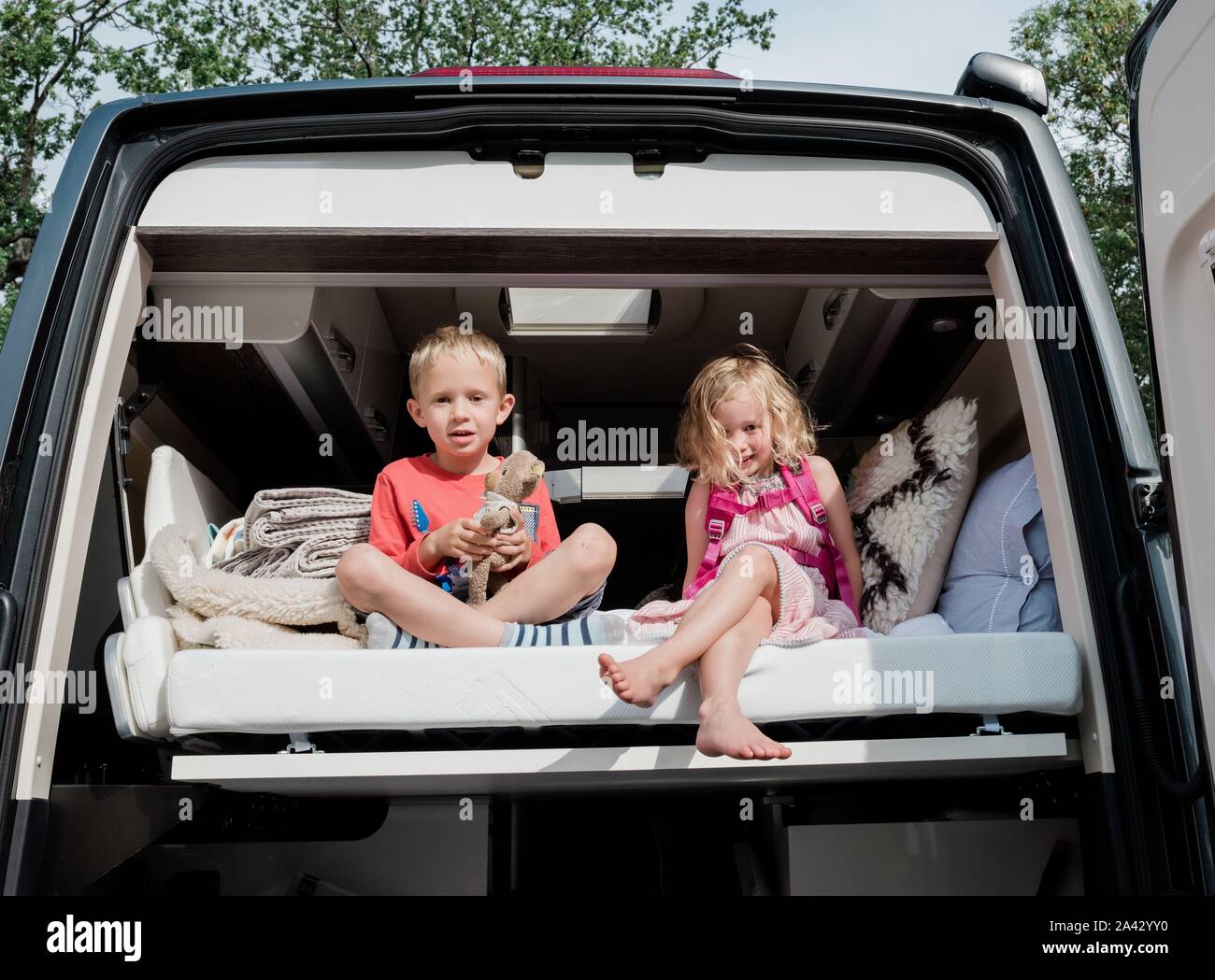brother and sister sat on a bed in a camper van on vacation in summer ...