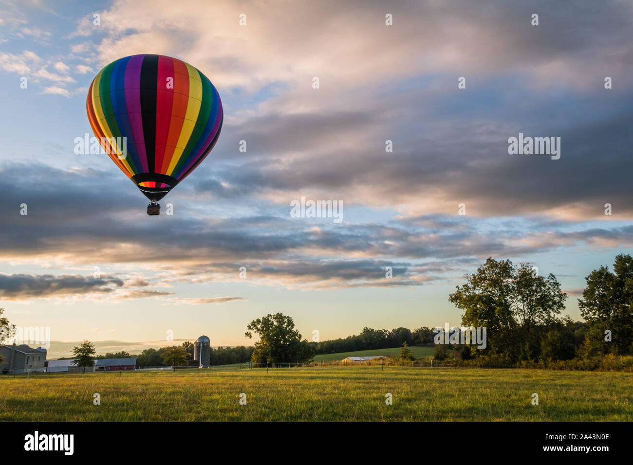 Rainbow hot-air balloon floats over field at sunrise Stock Photo - Alamy