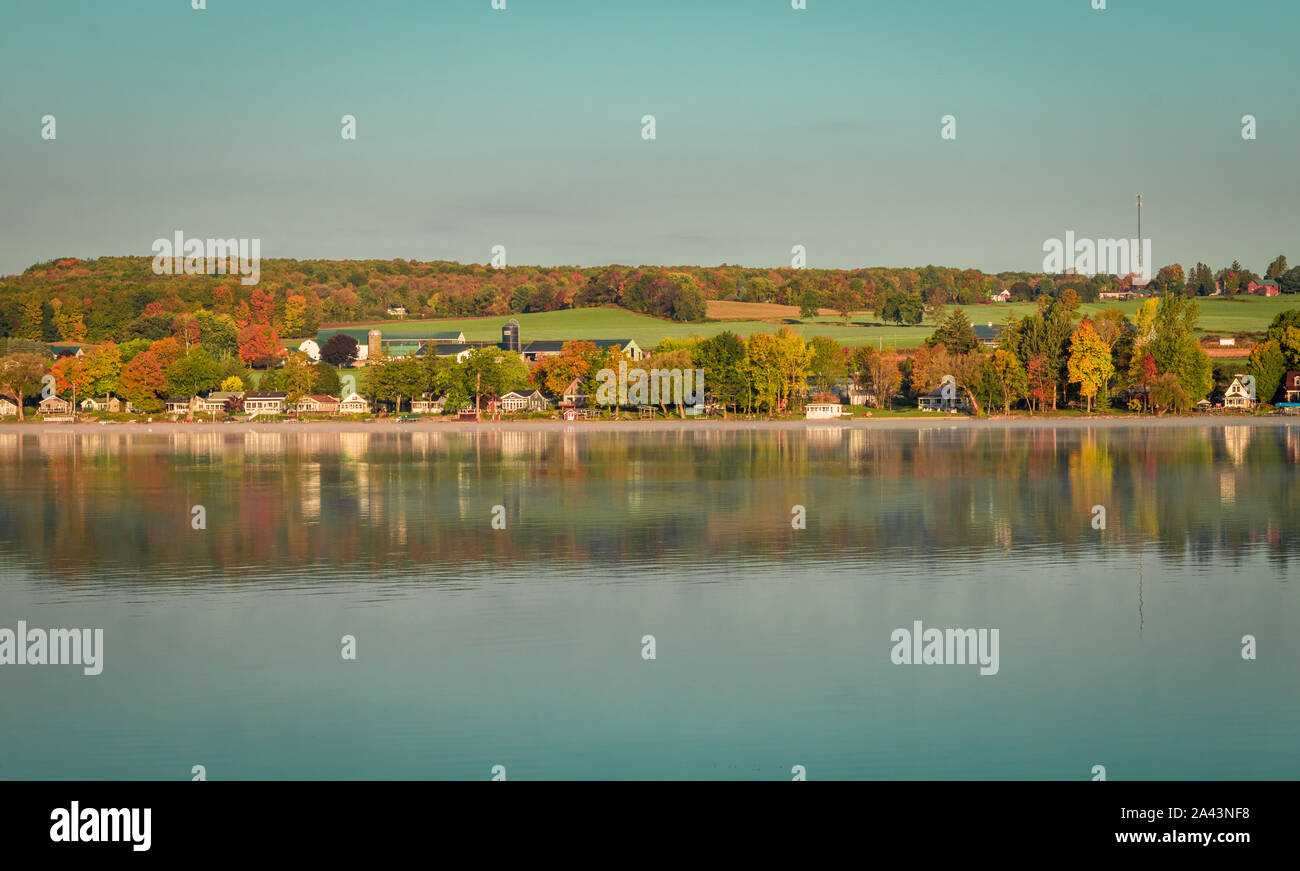 Fog rises over the lake at sunrise with lakefront cottages dotting the ...