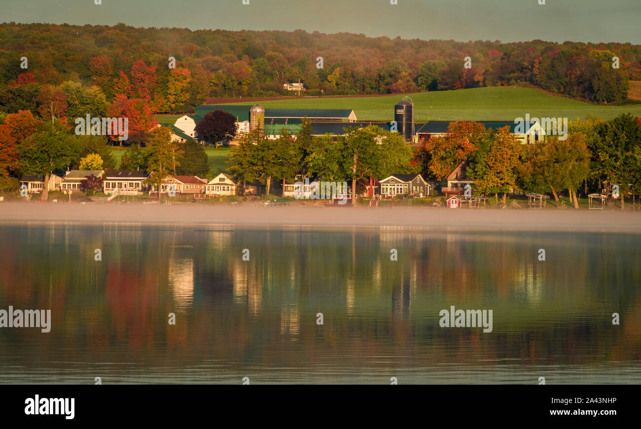 Fog rises over the lake at sunrise with lakefront cottages dotting the ...