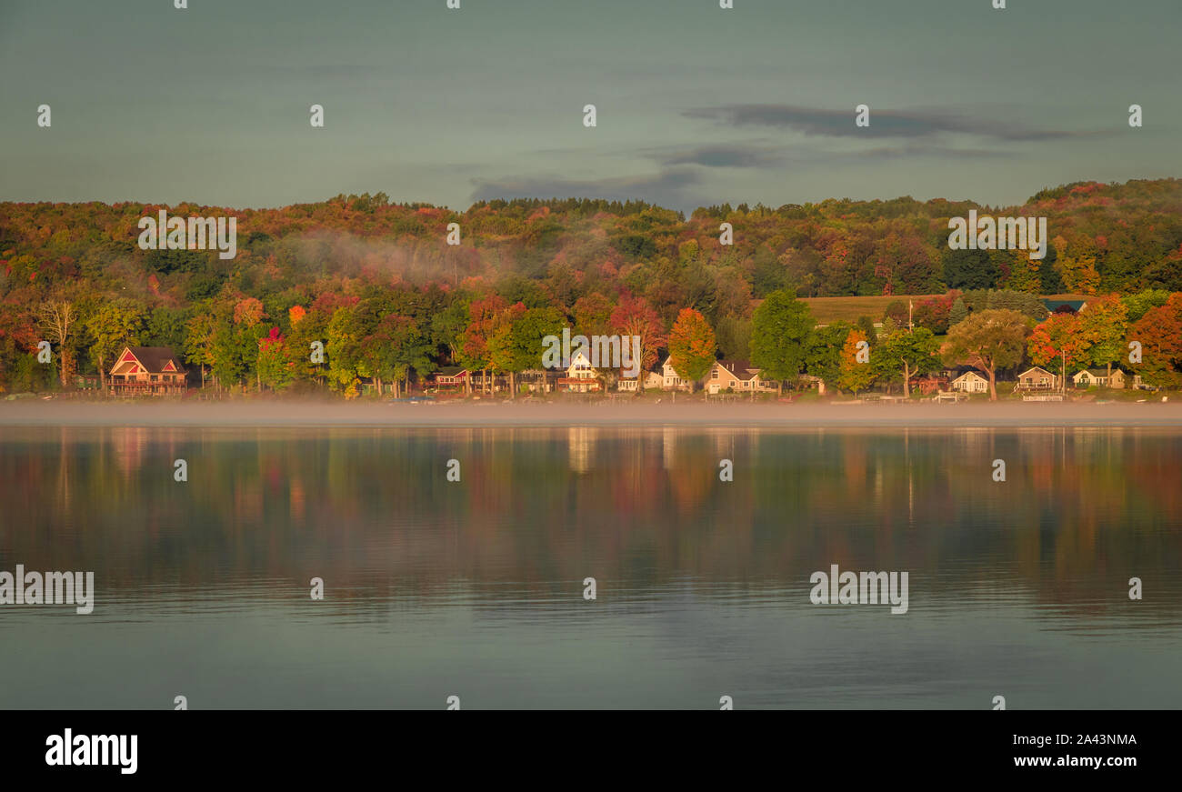 Fog rises over the lake at sunrise with lakefront cottages dotting the ...