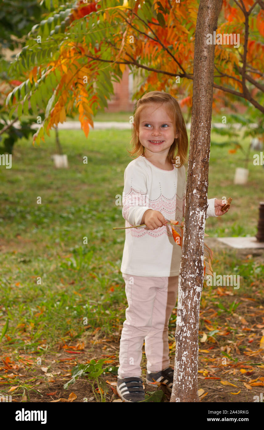 Adorable baby girl playing in a sunny park under a tree with yellow ...