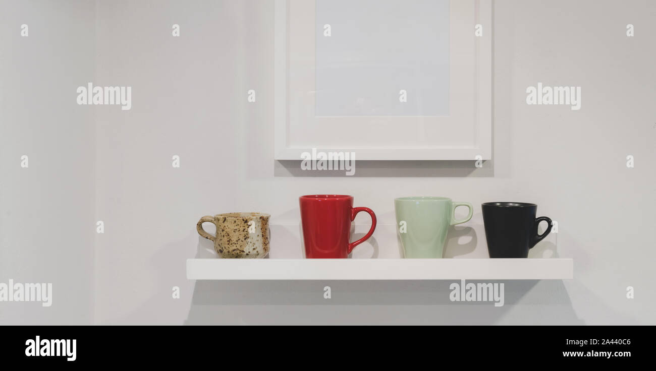 Cropped shot of wall shelf with coffee cups and mock up frame on white ...