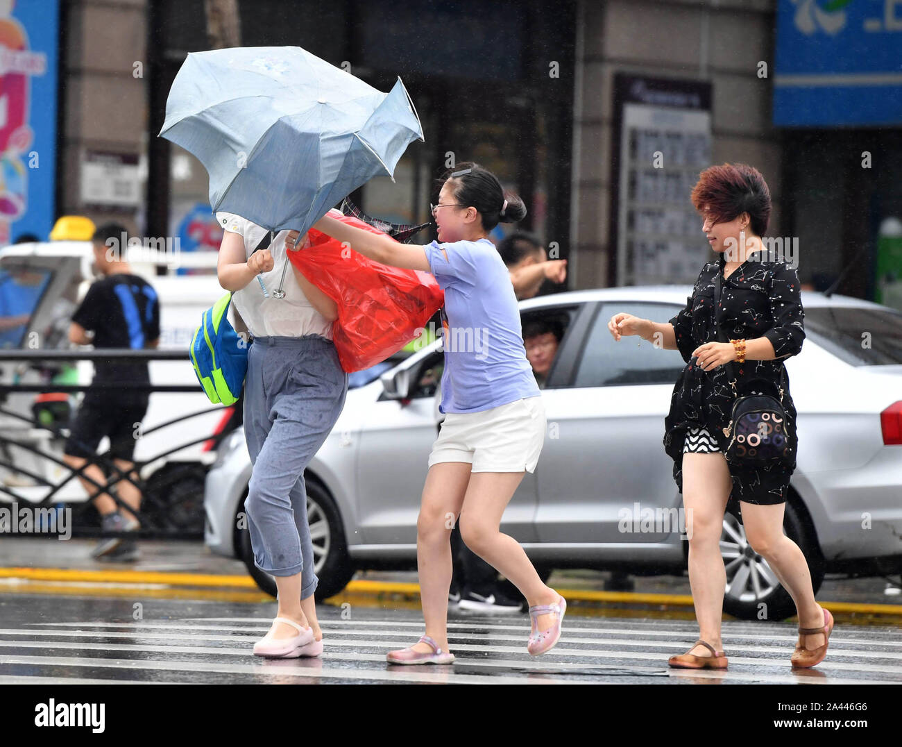 A local resident struggles with her umbrella in heavy rain and strong ...