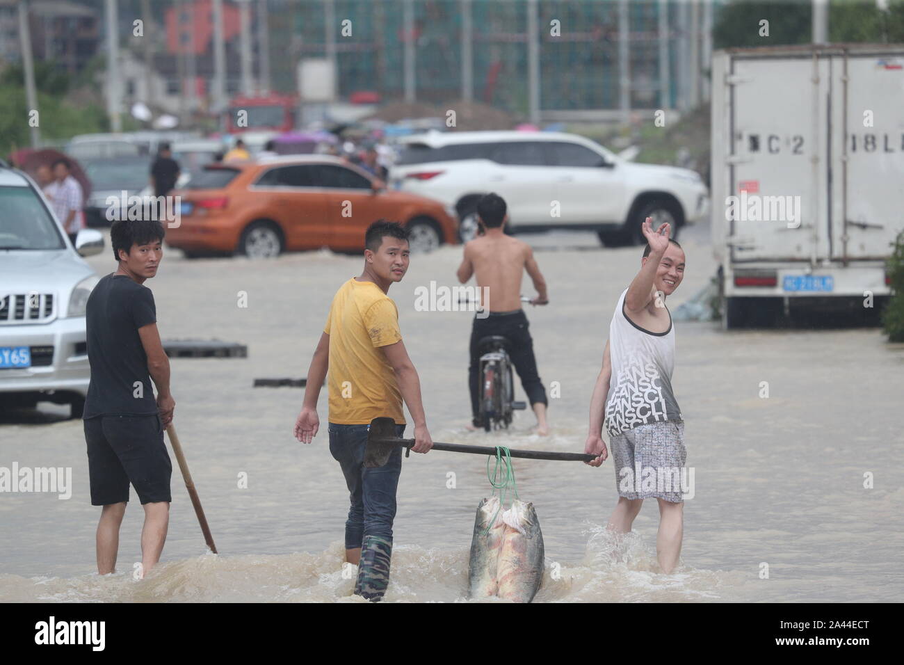Local residents carry fish as they walk on a flooded road after heavy ...