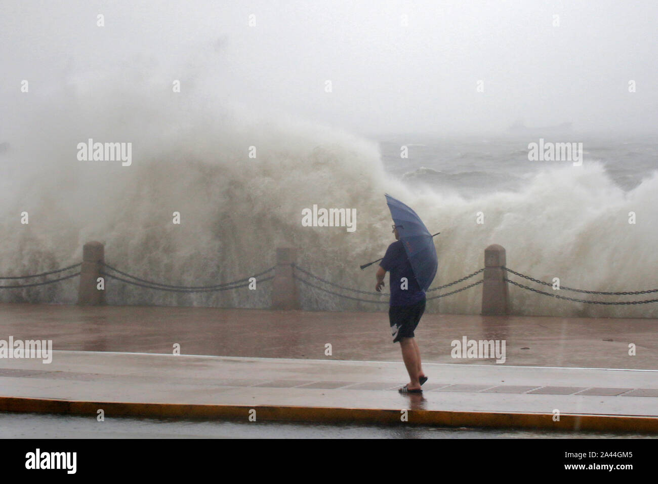 A local resident struggles with his umbrella in heavy rain and strong ...