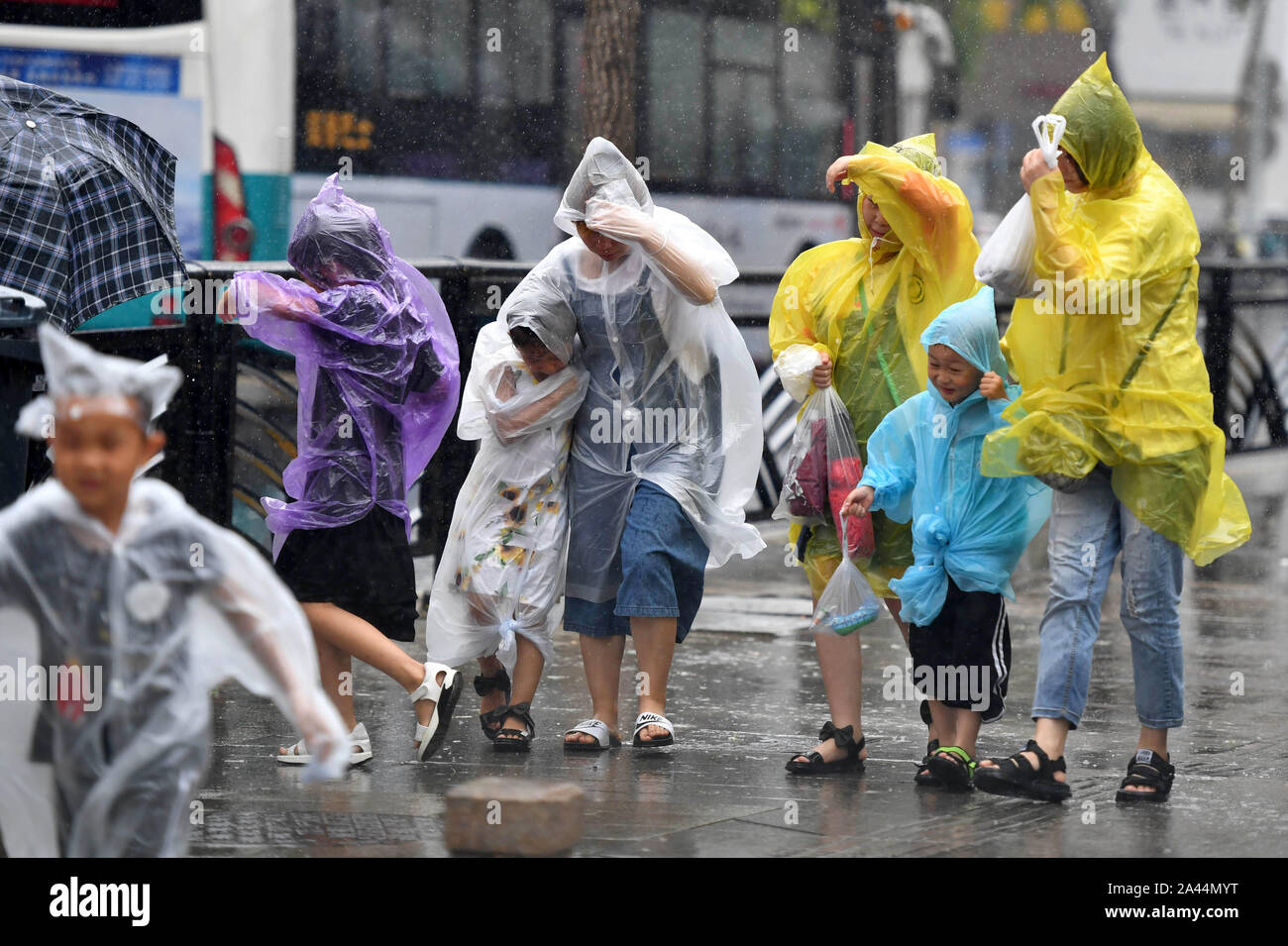 Local residents wearing raincoats walk against heavy rain and strong ...