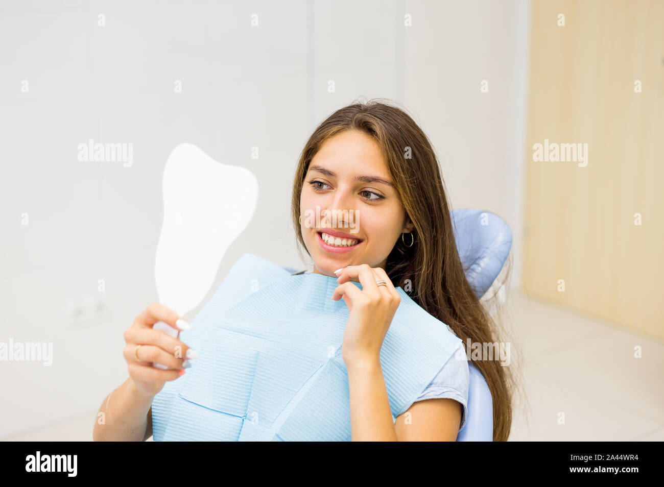The patient admires her smile looking at the mirror sitting in dental ...
