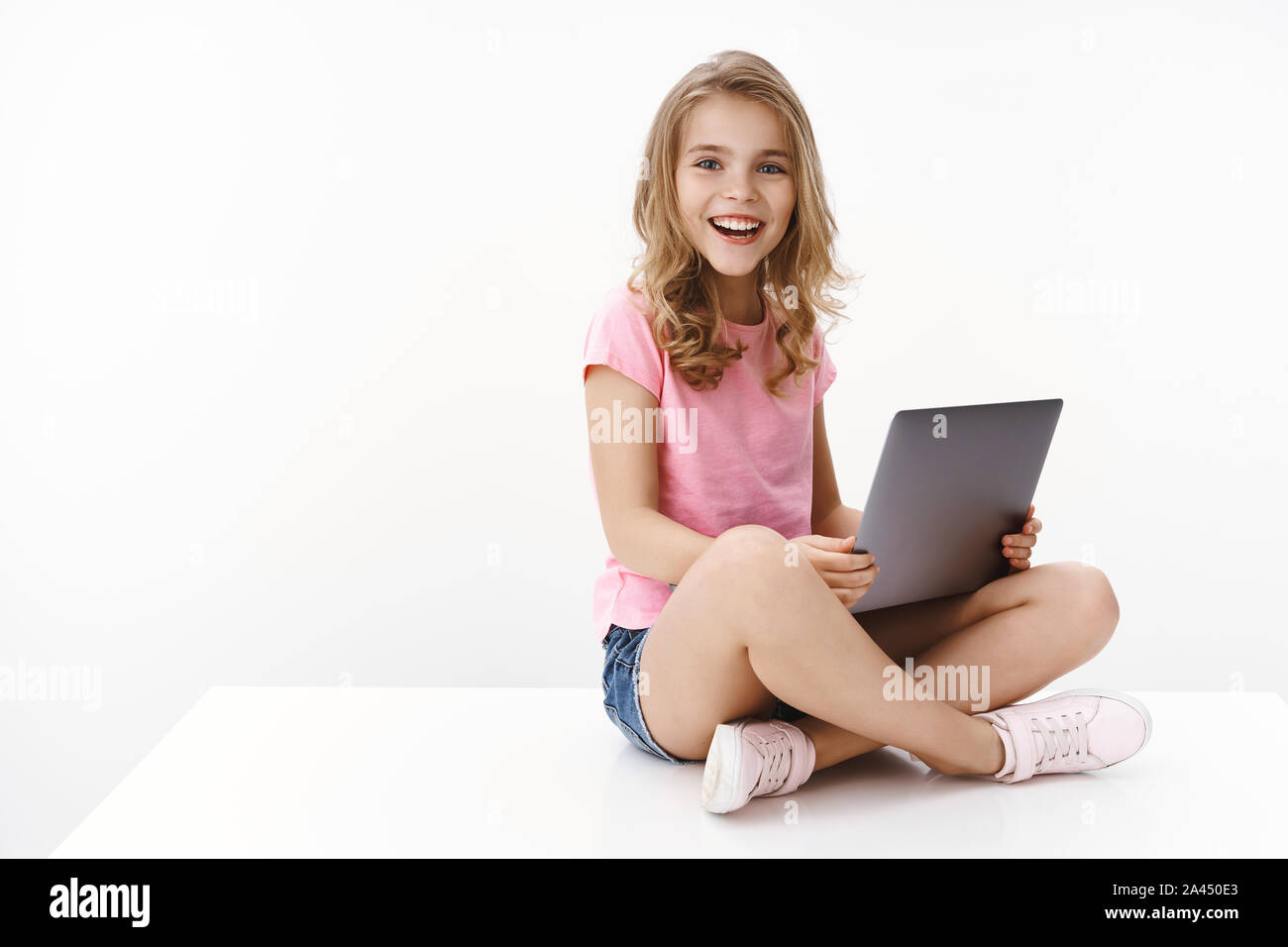 Pretty cheerful little kid girl sit crossed legs, hold laptop, studying ...