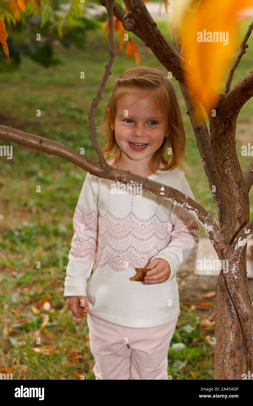 Adorable baby girl playing in a sunny park under a tree with yellow ...