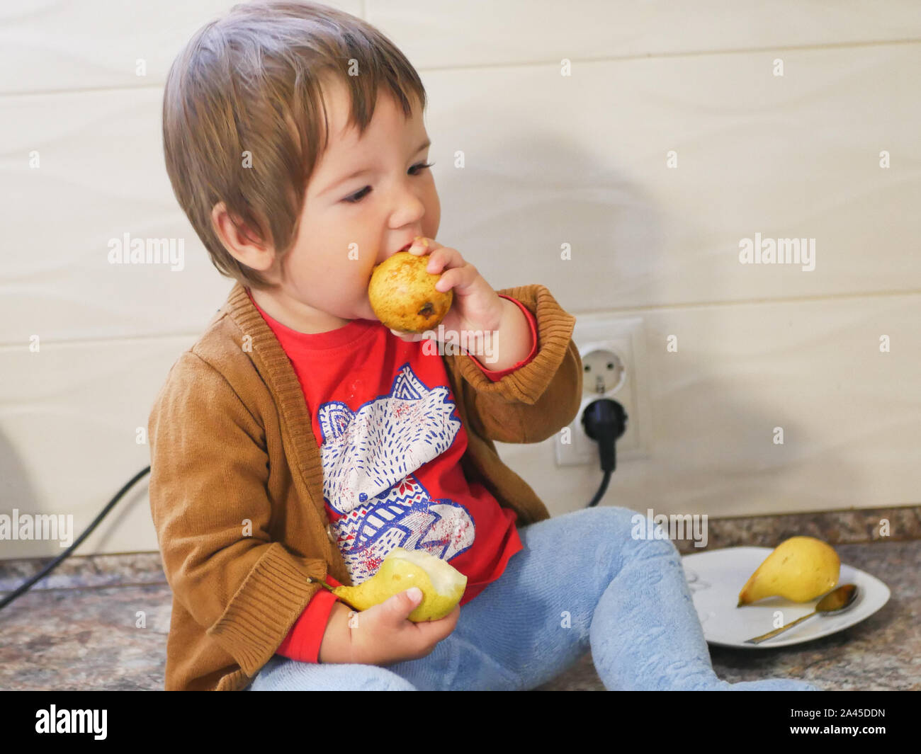 little child eats a pear. child boy eating fruits at a high stoic. in ...