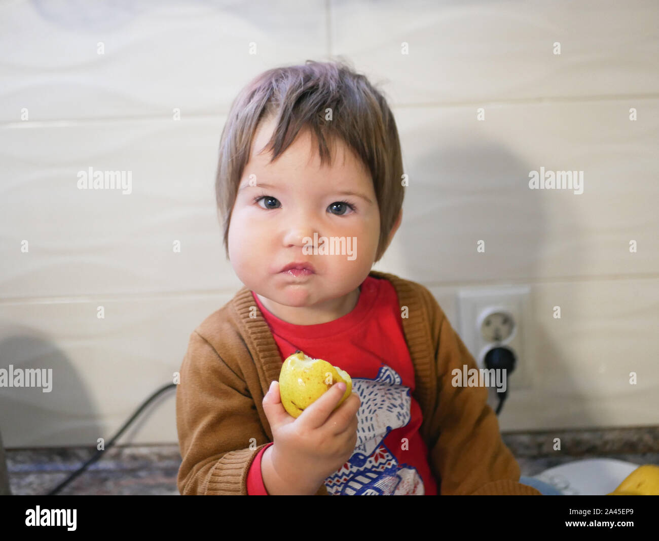 little child eats a pear. child boy eating fruits at a high stoic. in ...