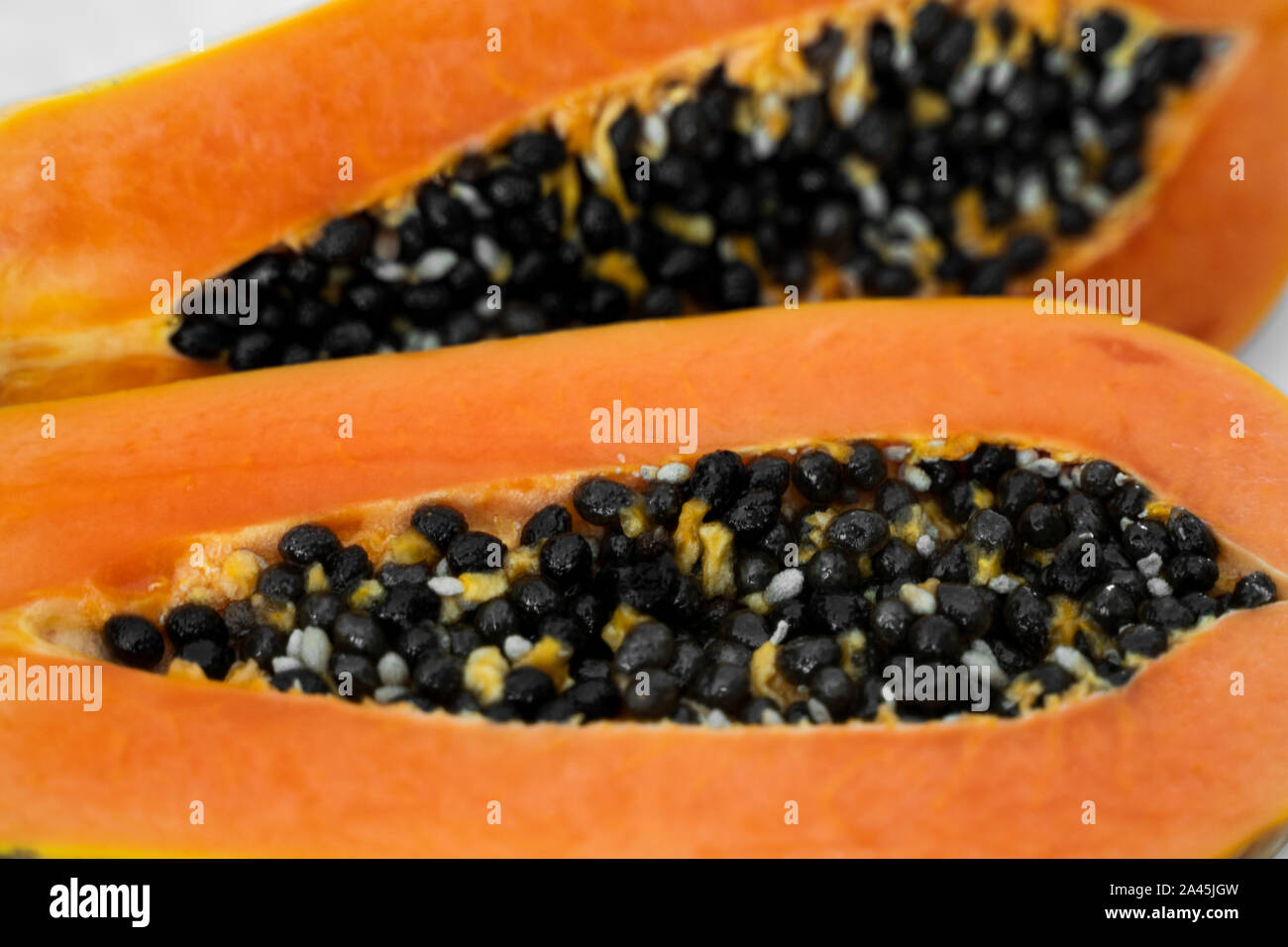 Half cut ripe papaya with seed on a white plate. Slices of sweet papaya ...